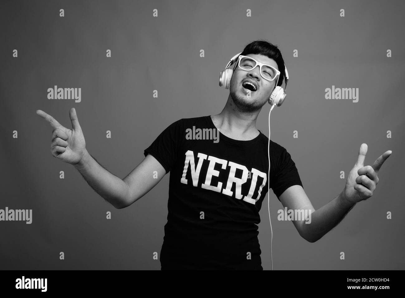 Young Asian nerd man listening to music against gray background Stock ...
