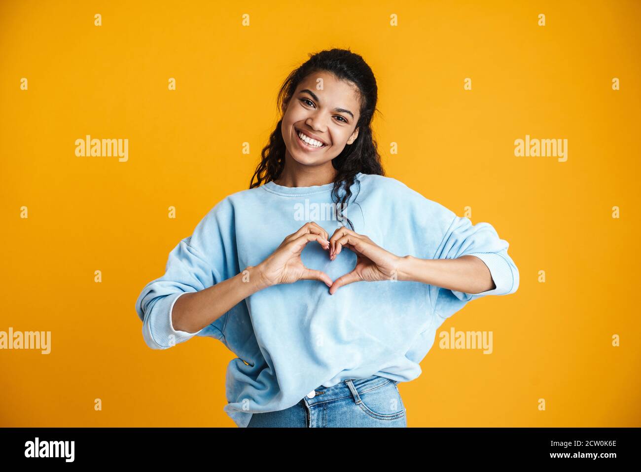 Beautiful african making heart symbol with hands isolated over yellow ...