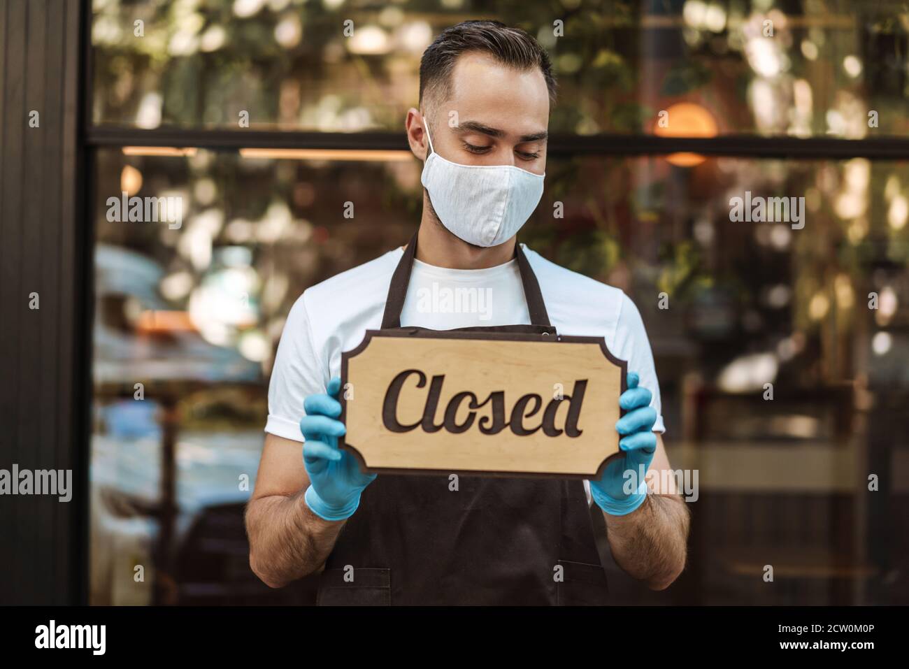 Upset man wearing medical face mask holding closed sign while standing ...