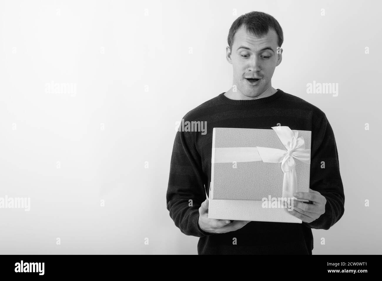 Studio shot of young muscular man opening gift box while looking ...