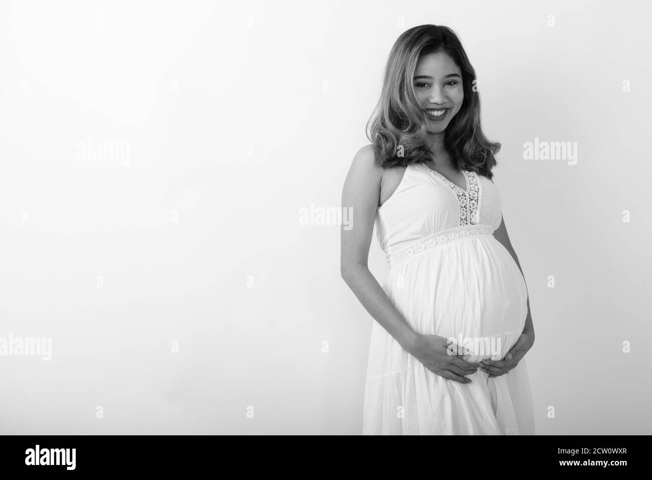 Studio shot of young happy Asian pregnant woman smiling while holding ...