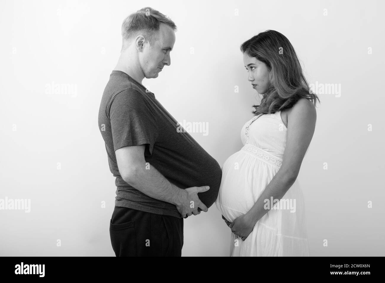 Profile view of young multi ethnic married couple touching tummies ...