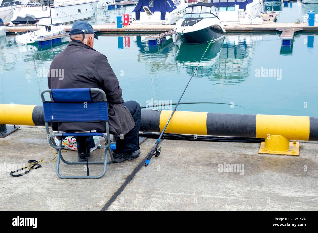 Fisherman old man sitting with fishing rod in the seaport on the Black ...