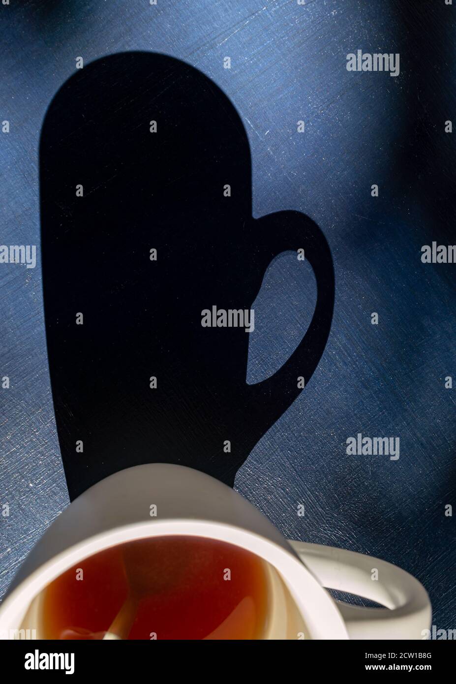 White tea mug casting a dark shadow on a dark blue wood texture ...