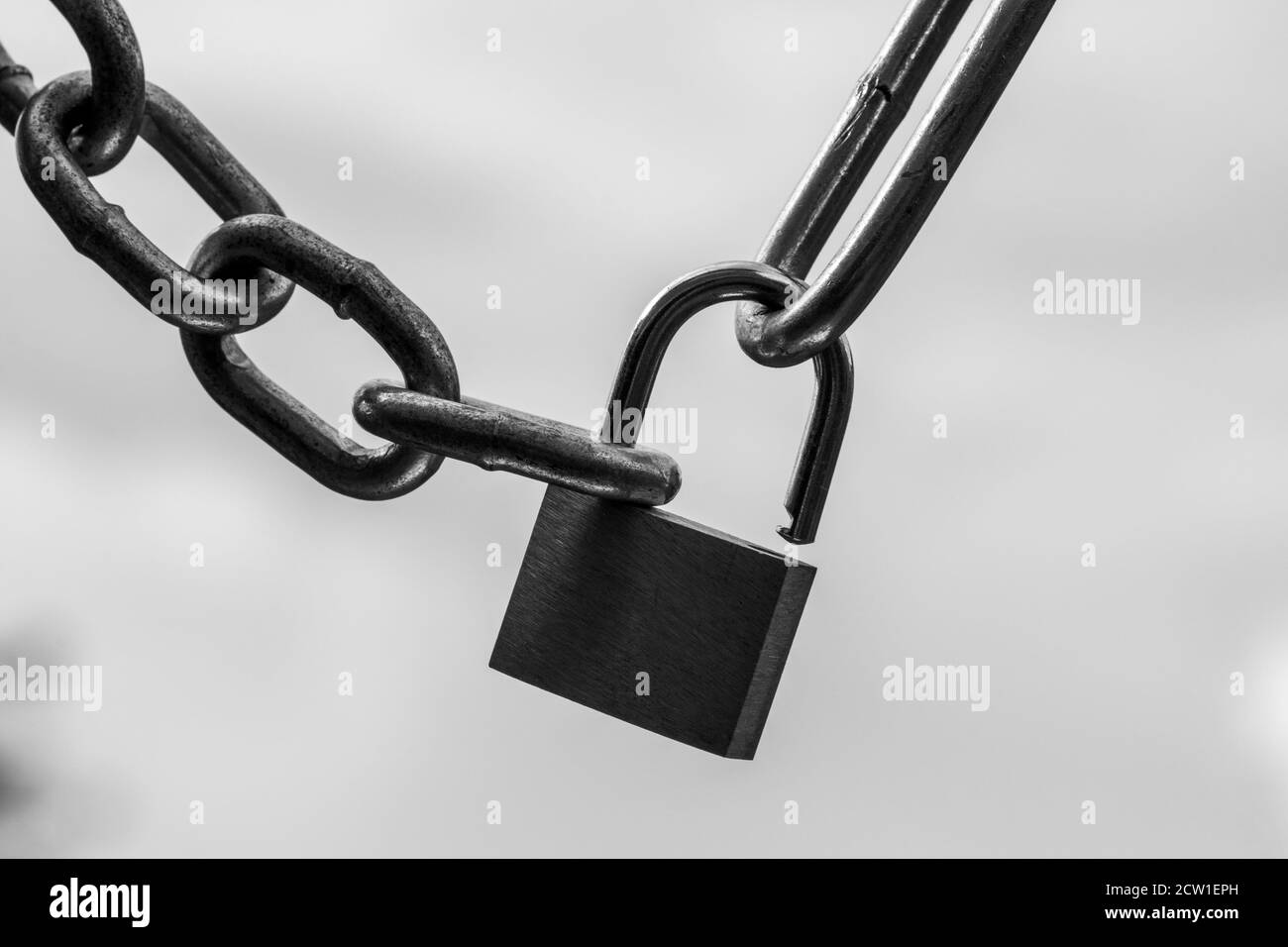 Chrome padlock and steel chains close up against blue clouded sky ...