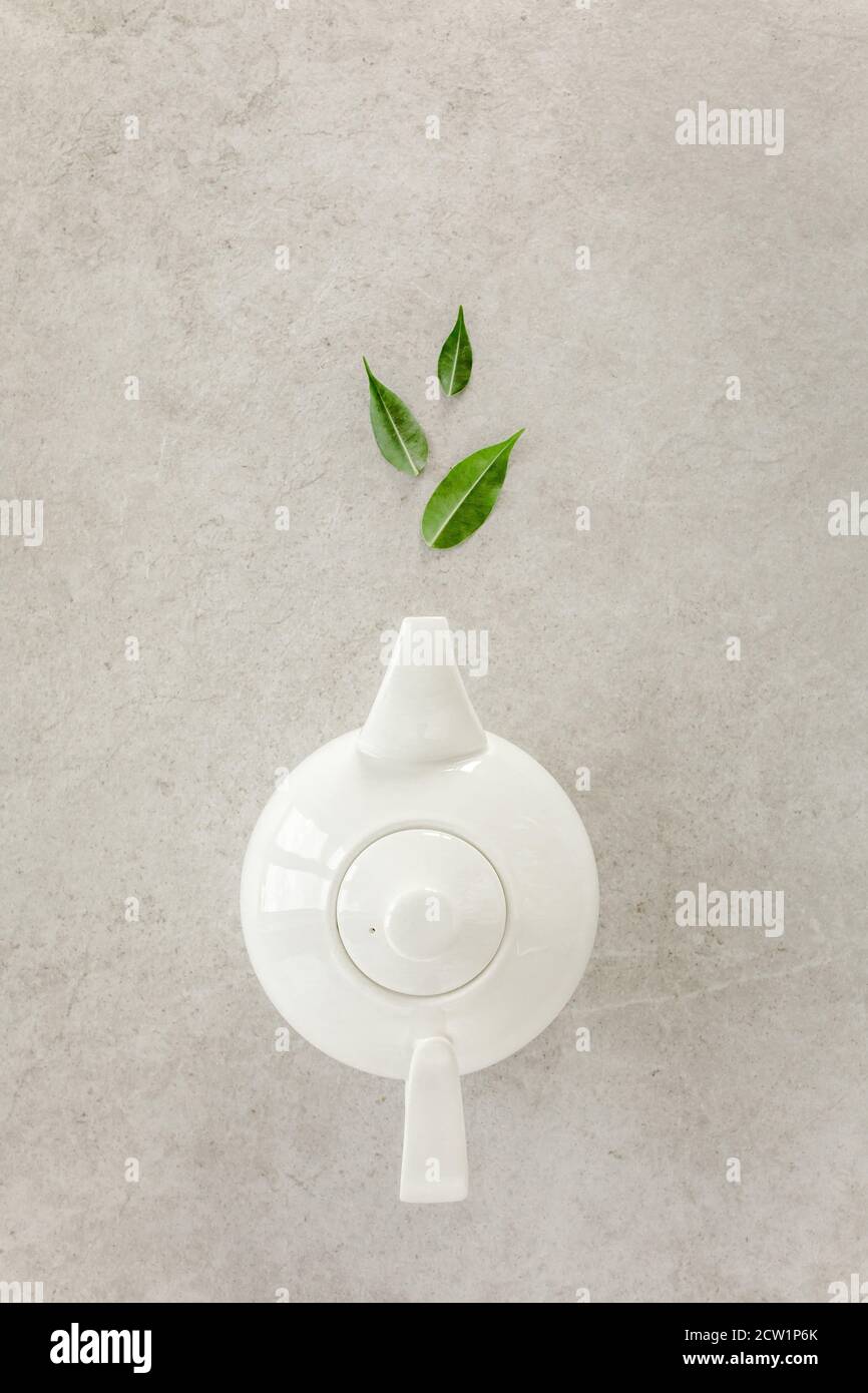 Herbal tea in a white teapot, with green tea leaves. Flat lay, top view ...