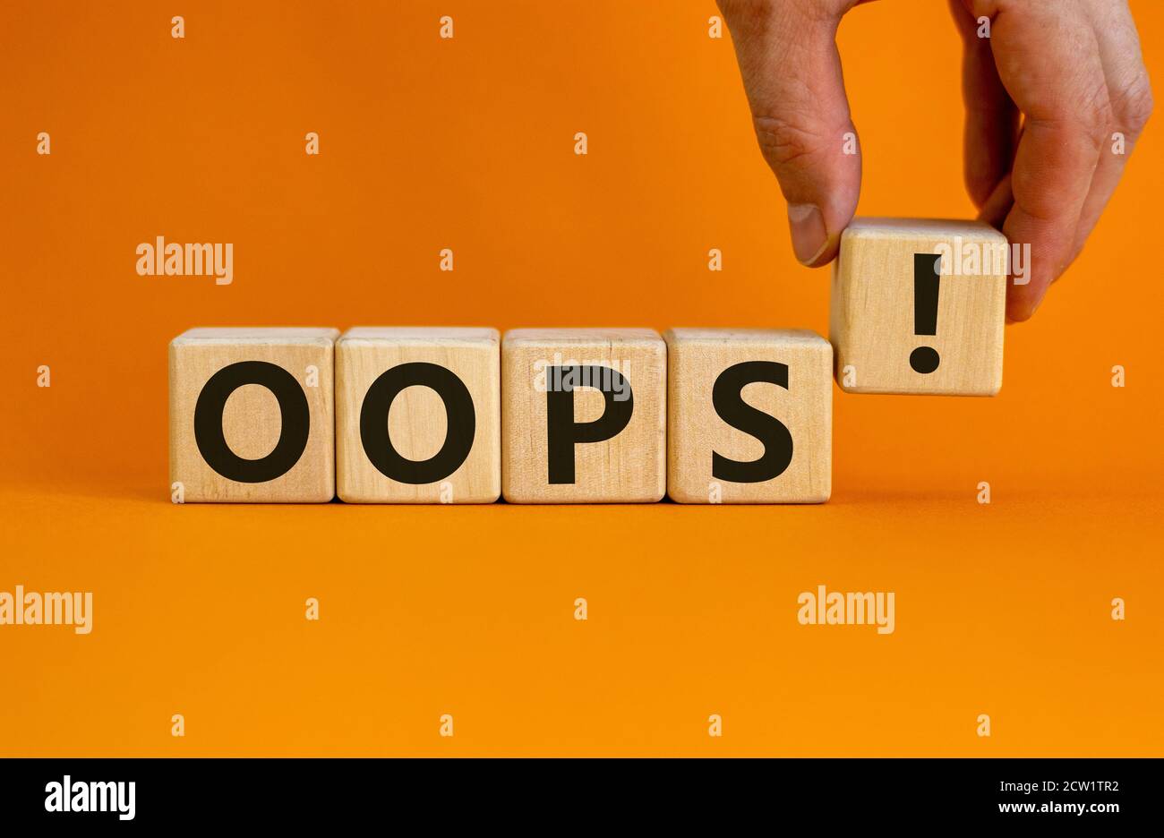 Oops sign on wooden cubes. Male hand. Beautiful orange background, copy ...