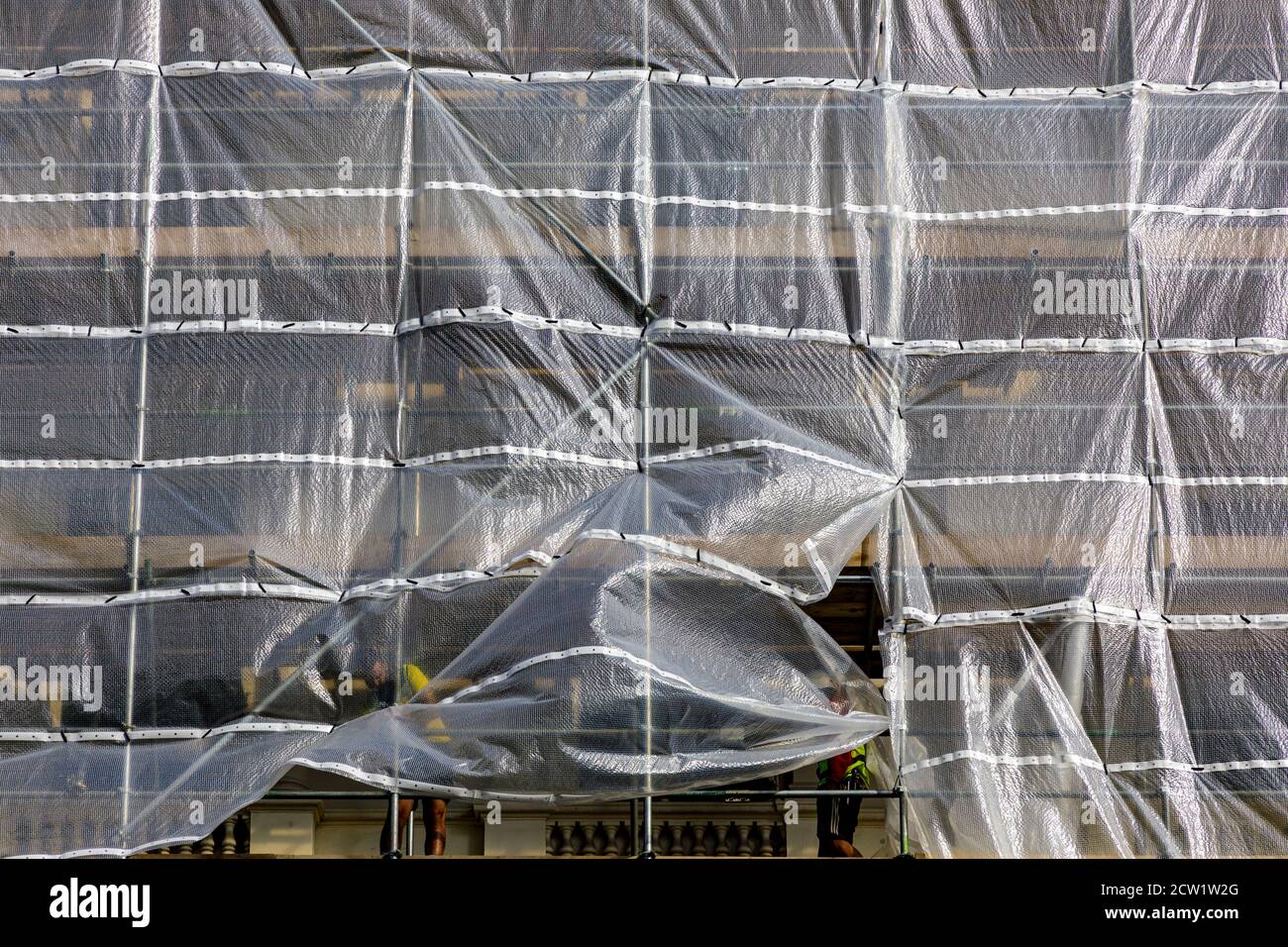 Workers struggle with the wind to tie a cover over the scaffold on the ...
