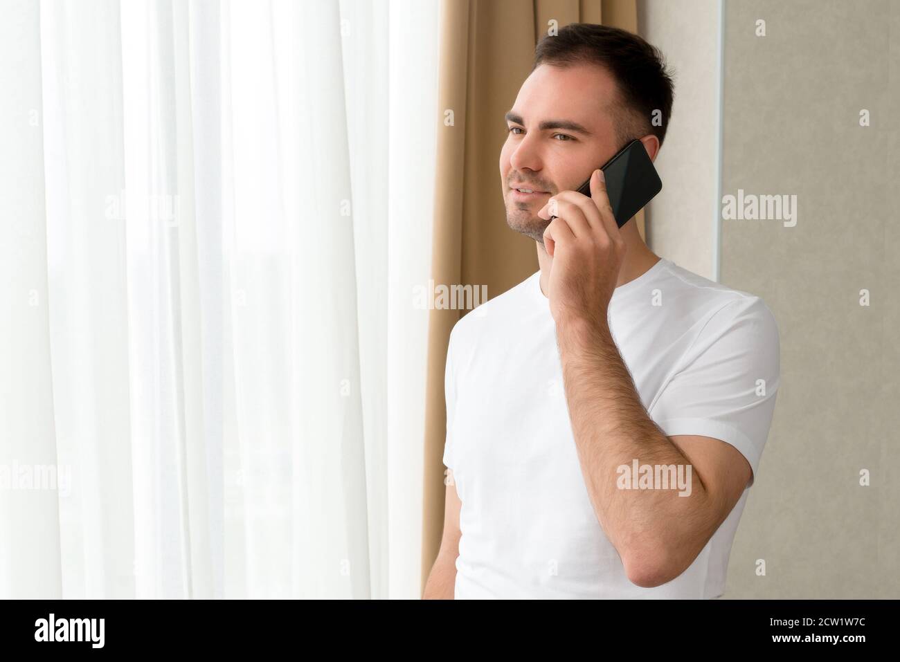 Handsome Caucasian man looking through window in hotel while speaking ...