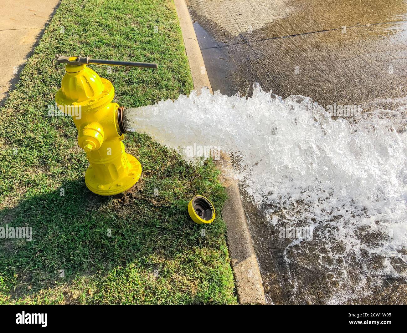 Side view opened yellow fire hydrant gushing water across a residential ...