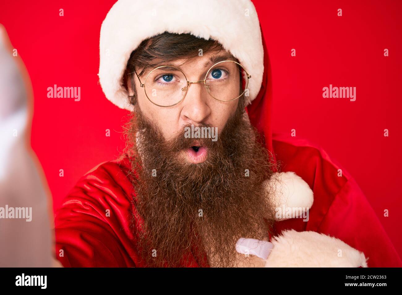 Handsome young red head man with long beard wearing santa claus costume ...