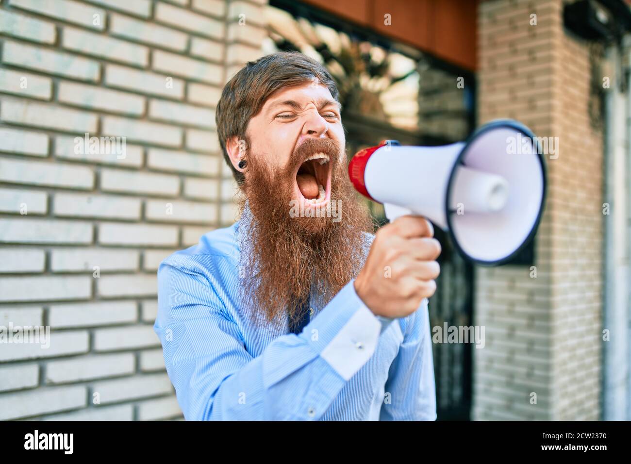 Young redhead businessman with angry expression. Screaming using ...