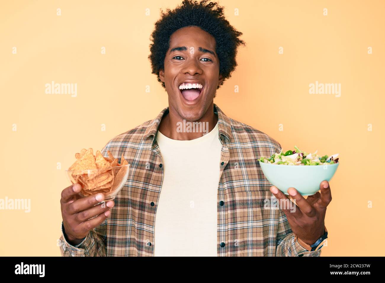 Handsome african american man with afro hair holding nachos and healthy ...