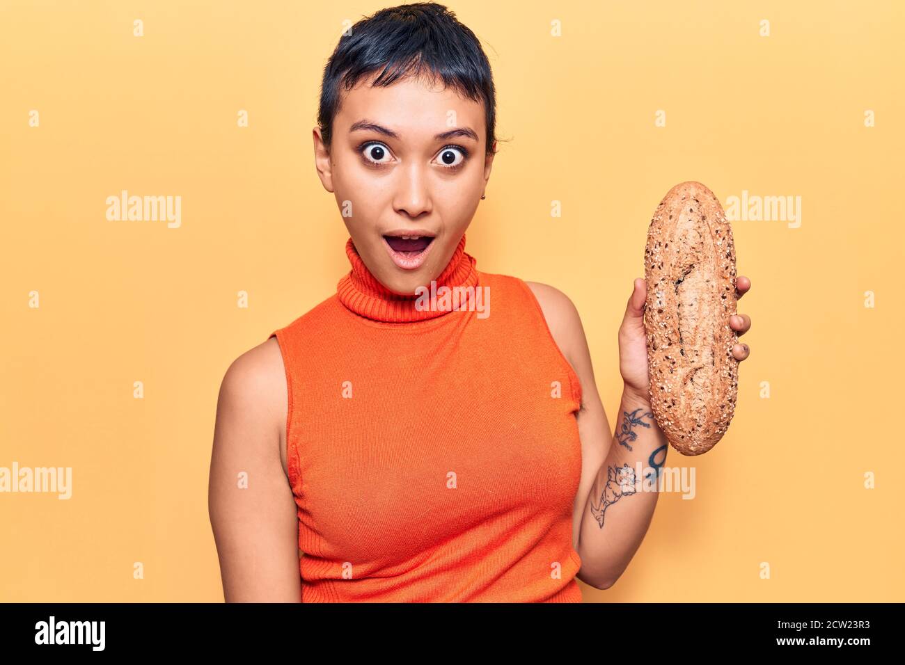 Young woman holding wholemeal bread scared and amazed with open mouth ...