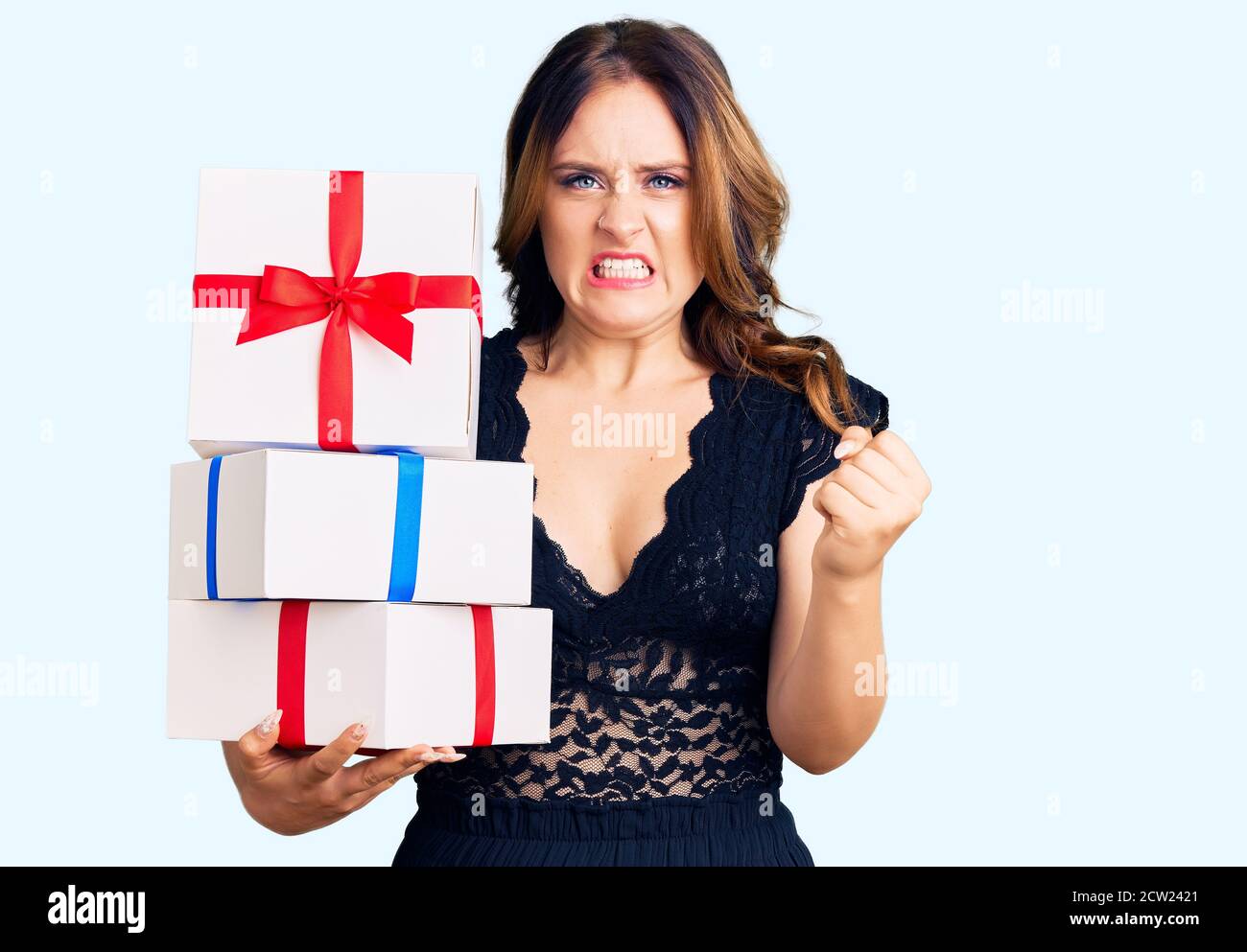 Young beautiful caucasian woman holding gifts annoyed and frustrated ...