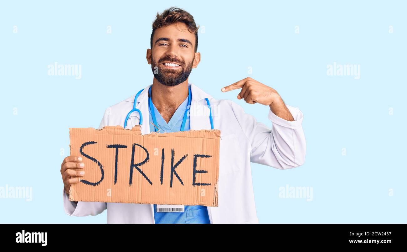 Young hispanic man wearing doctor stethoscope holding strike banner ...