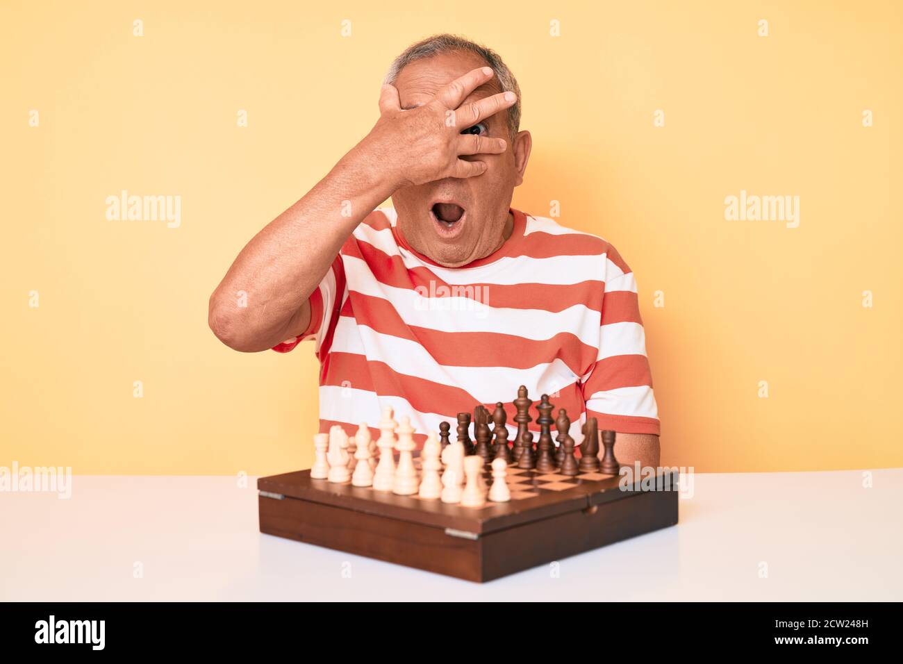 Senior handsome man with gray hair playing chess sitting on the table ...