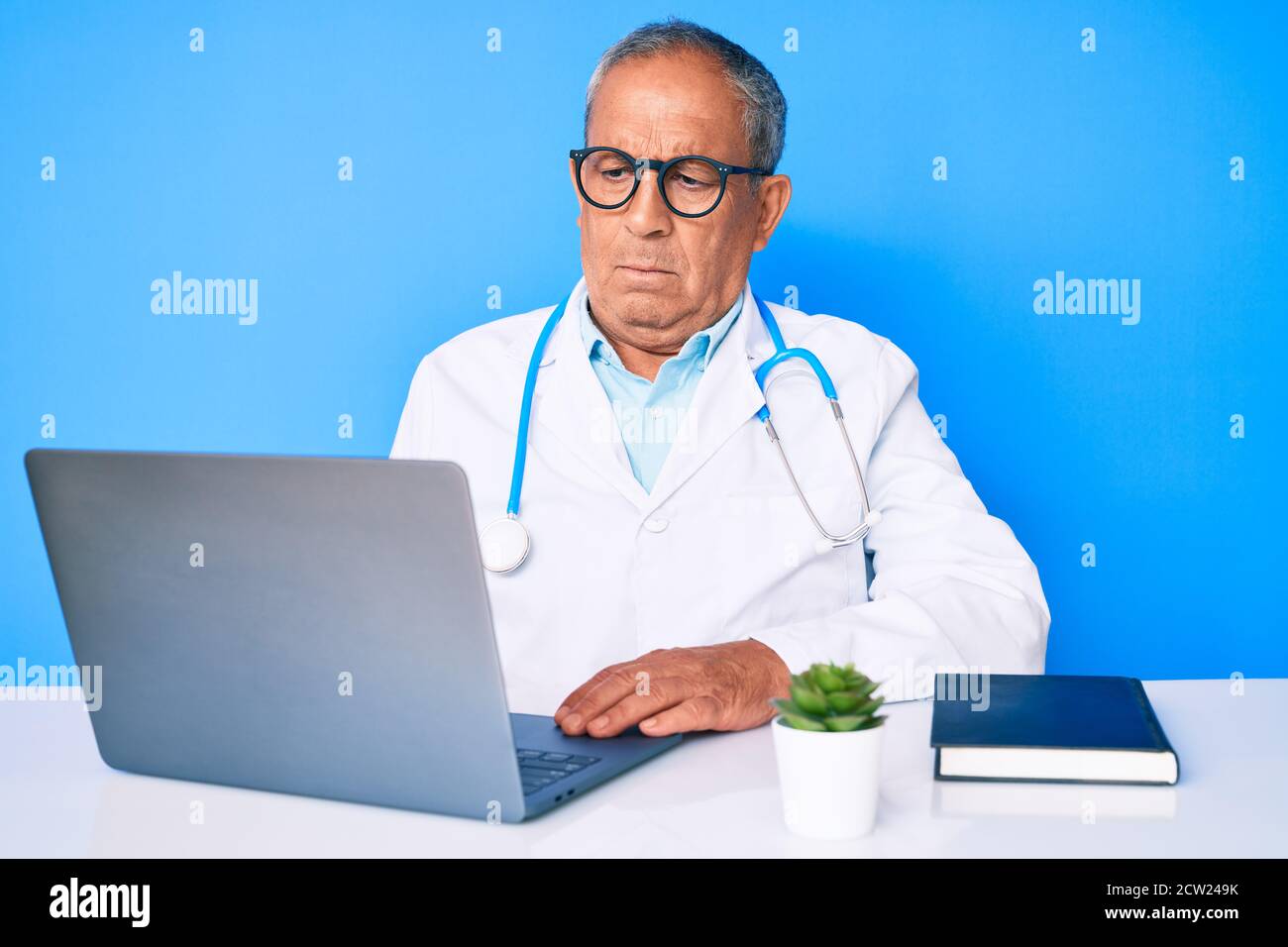 Senior handsome man with gray hair wearing doctor uniform working using ...