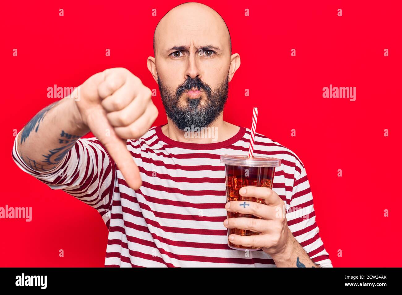 Young handsome man drinking glass of cola beverage with angry face ...