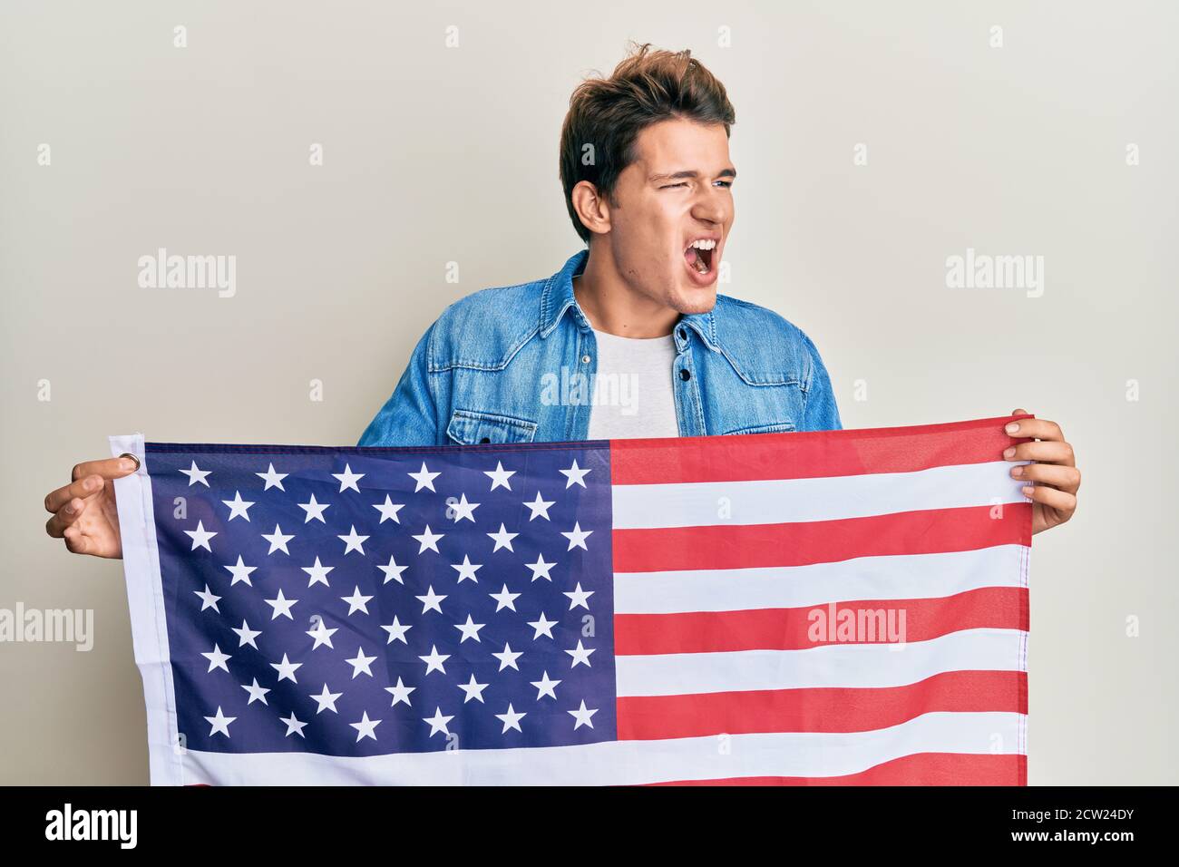 Handsome caucasian man holding united states flag angry and mad ...