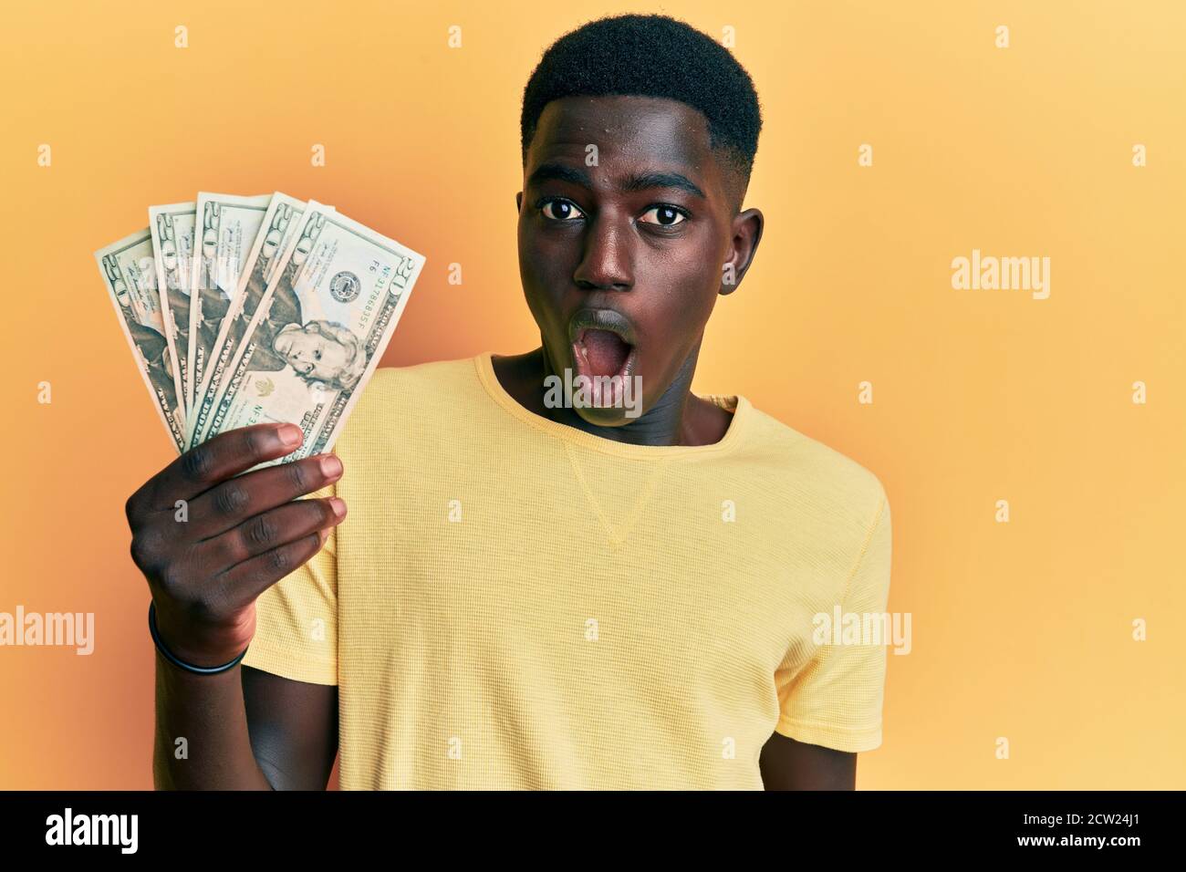 Young african american man holding dollars scared and amazed with open ...
