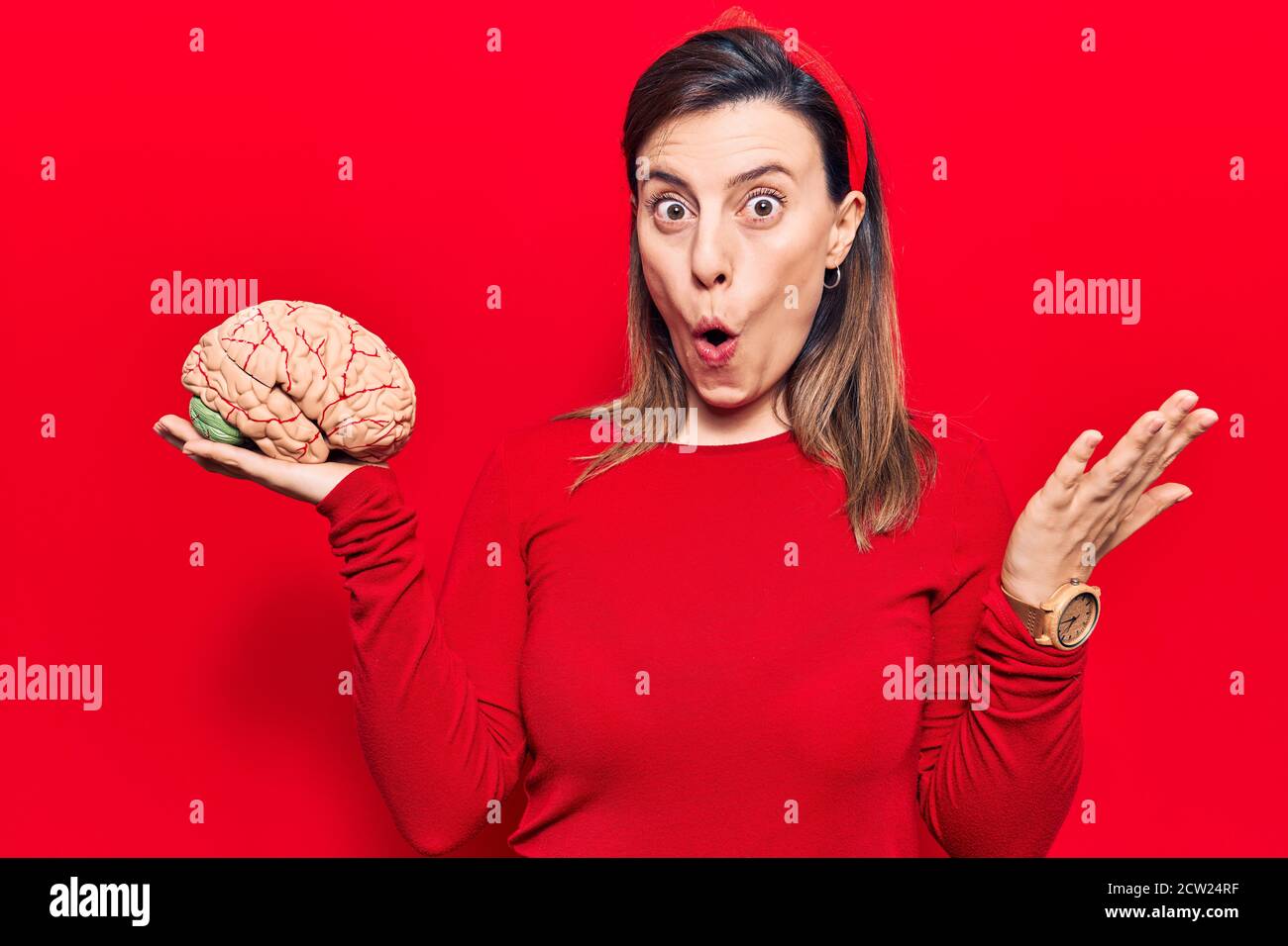 Young beautiful woman holding brain scared and amazed with open mouth ...