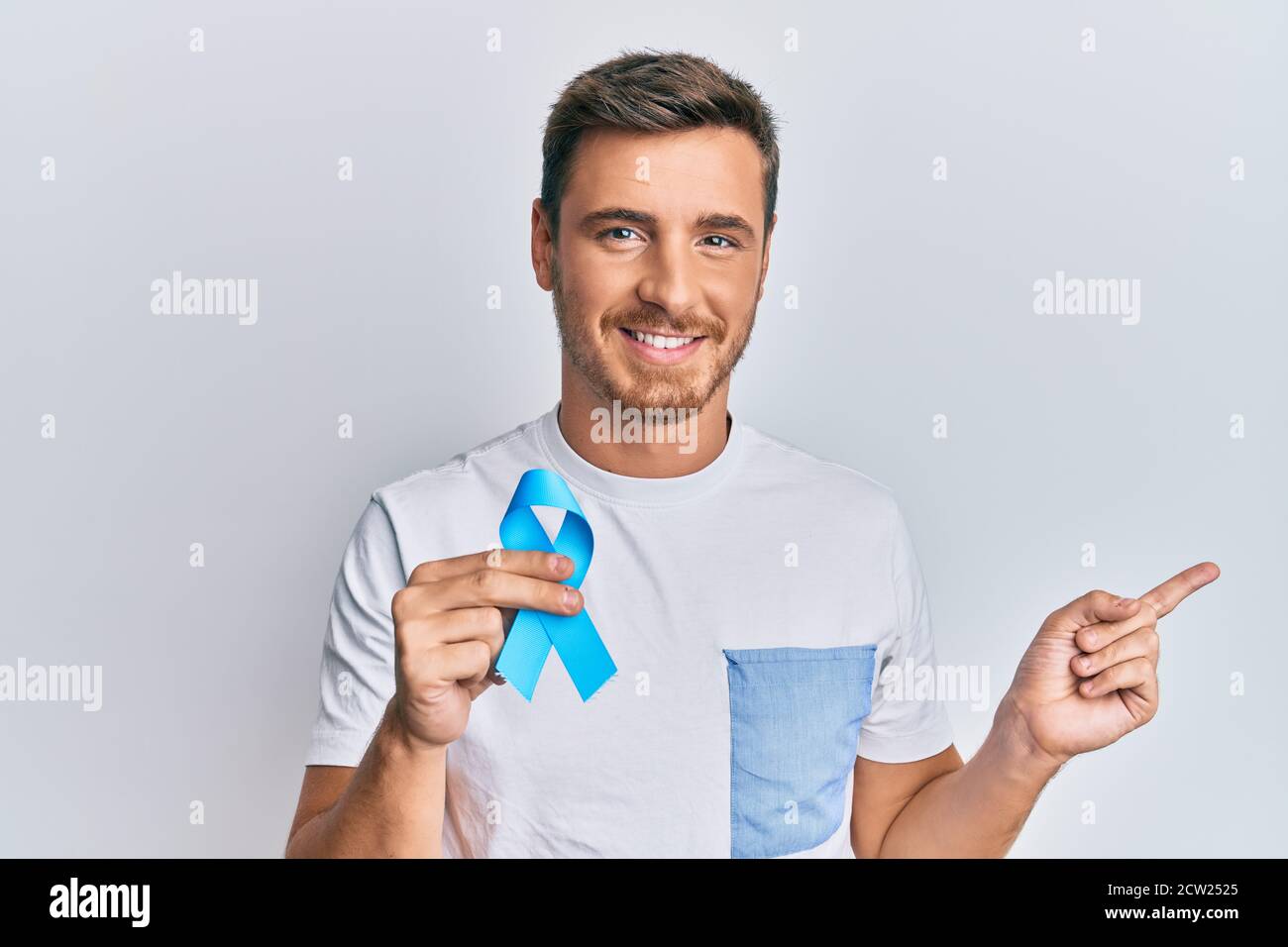 Handsome caucasian man holding blue ribbon smiling happy pointing with ...