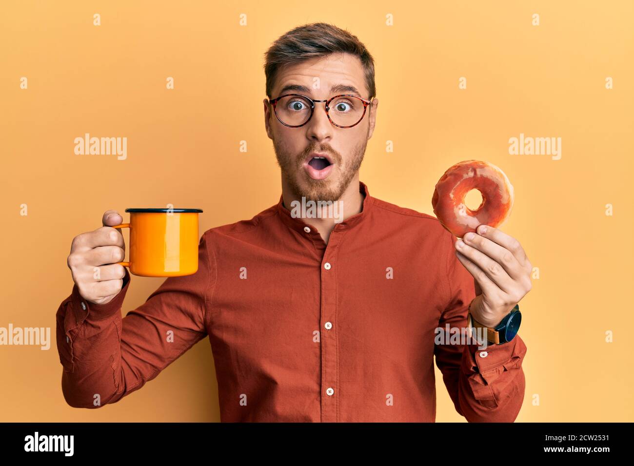 Handsome caucasian man eating doughnut and drinking coffee afraid and ...