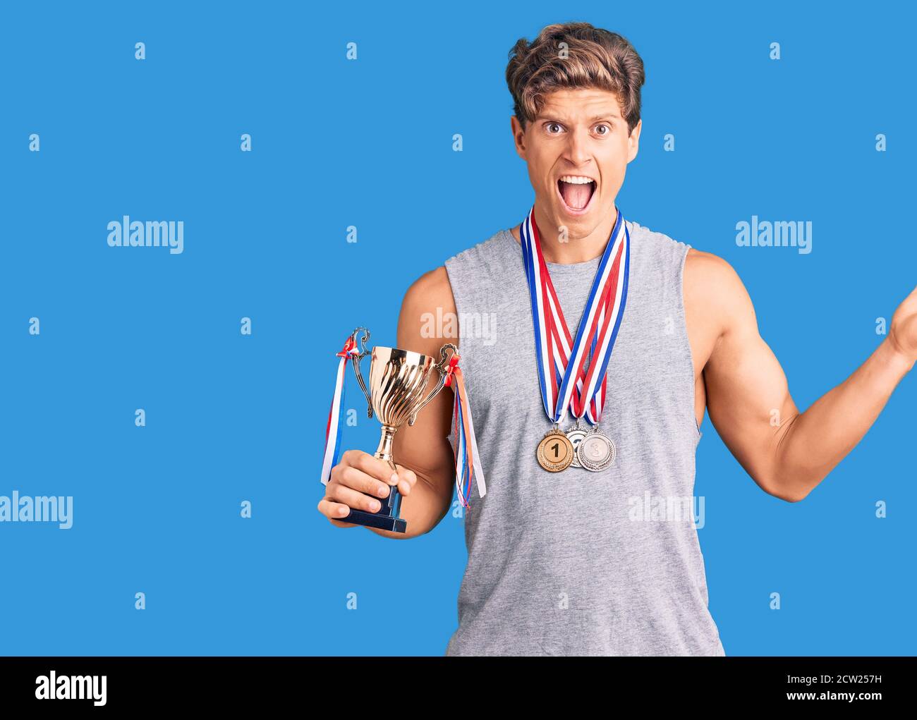Young handsome man holding champion trophy wearing medals celebrating ...