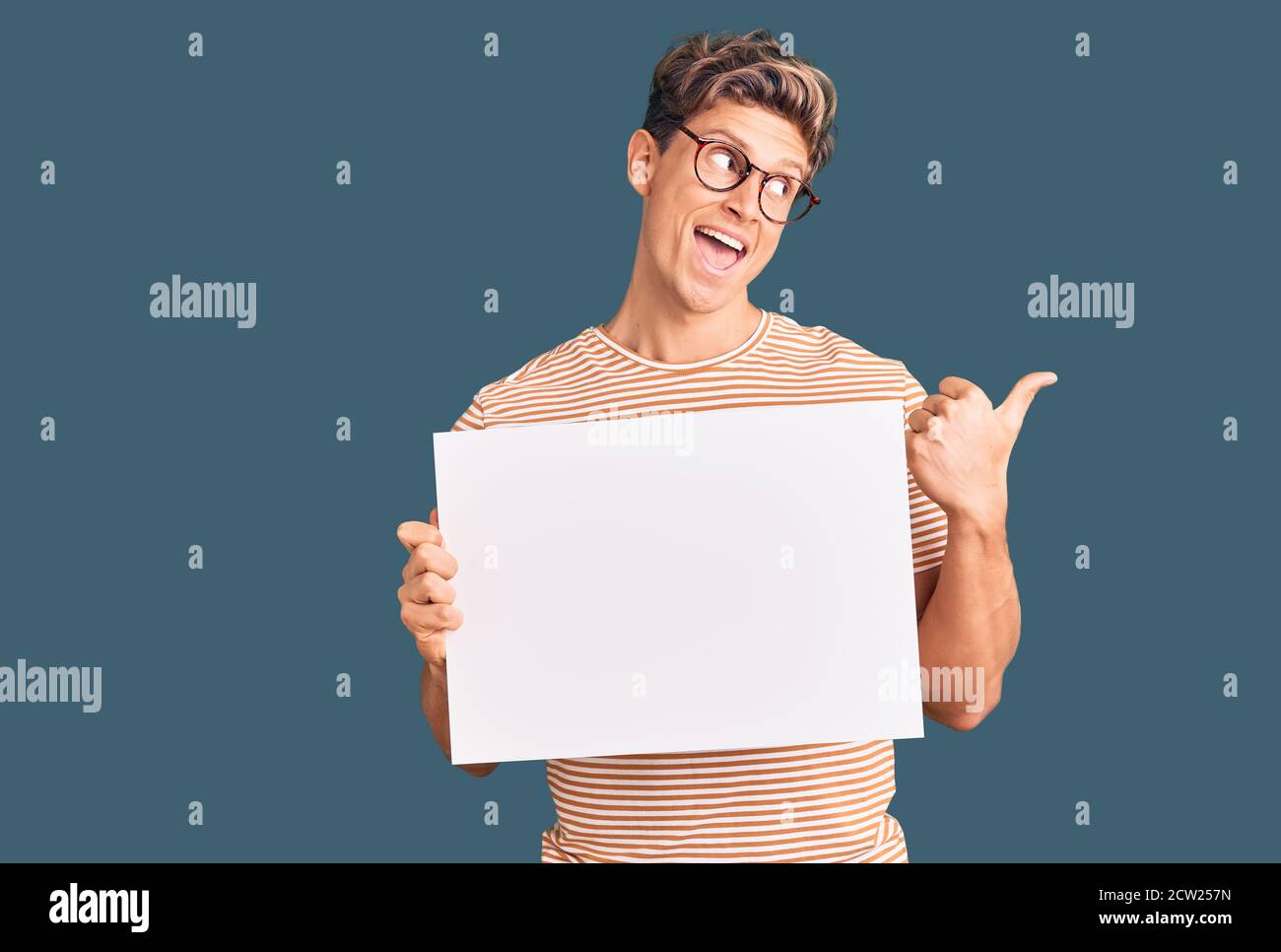 Young Handsome Man Holding Blank Empty Banner Pointing Thumb Up To The