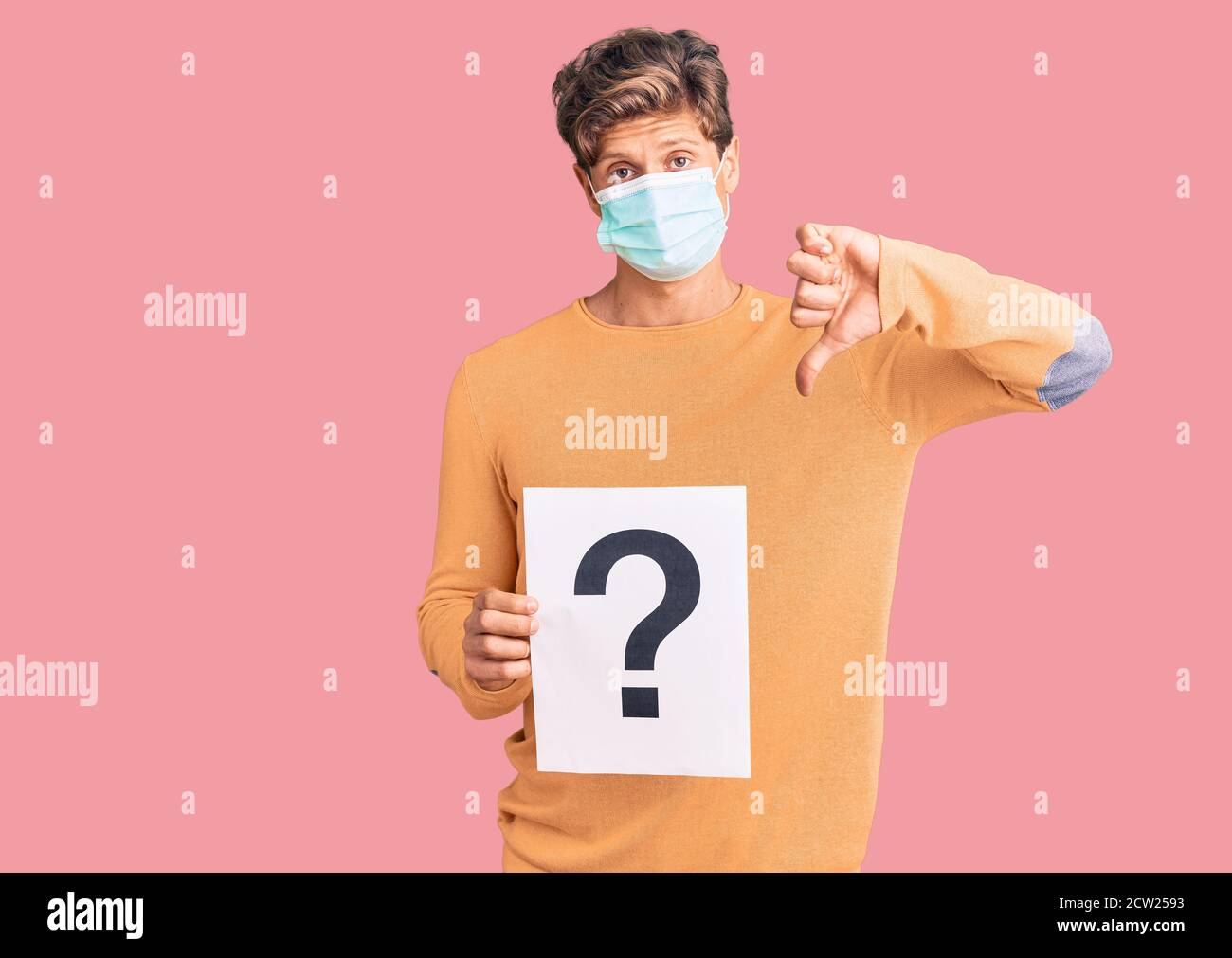 Young handsome man wearing medical mask holding question mark with ...
