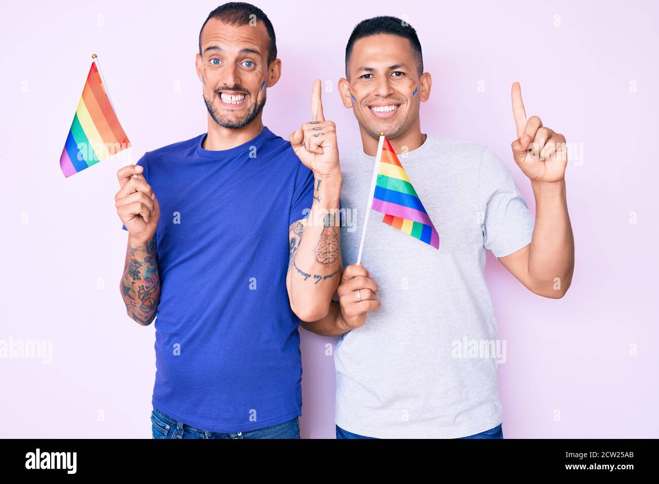 Young gay couple of two men holding rainbow lgbtq flags together ...