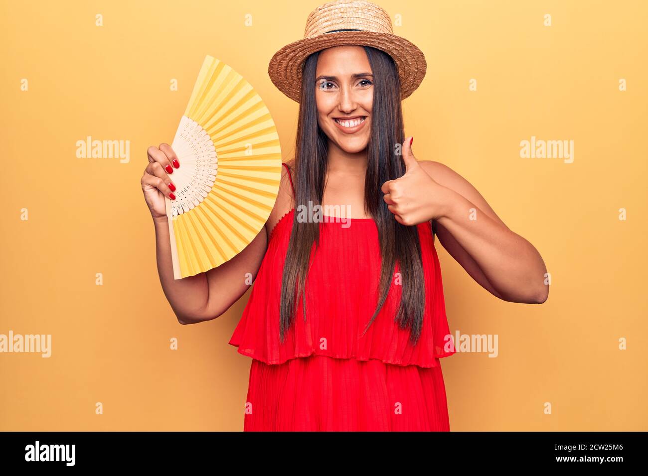 Young beautiful brunette woman wearing summer hat holding hand fan ...