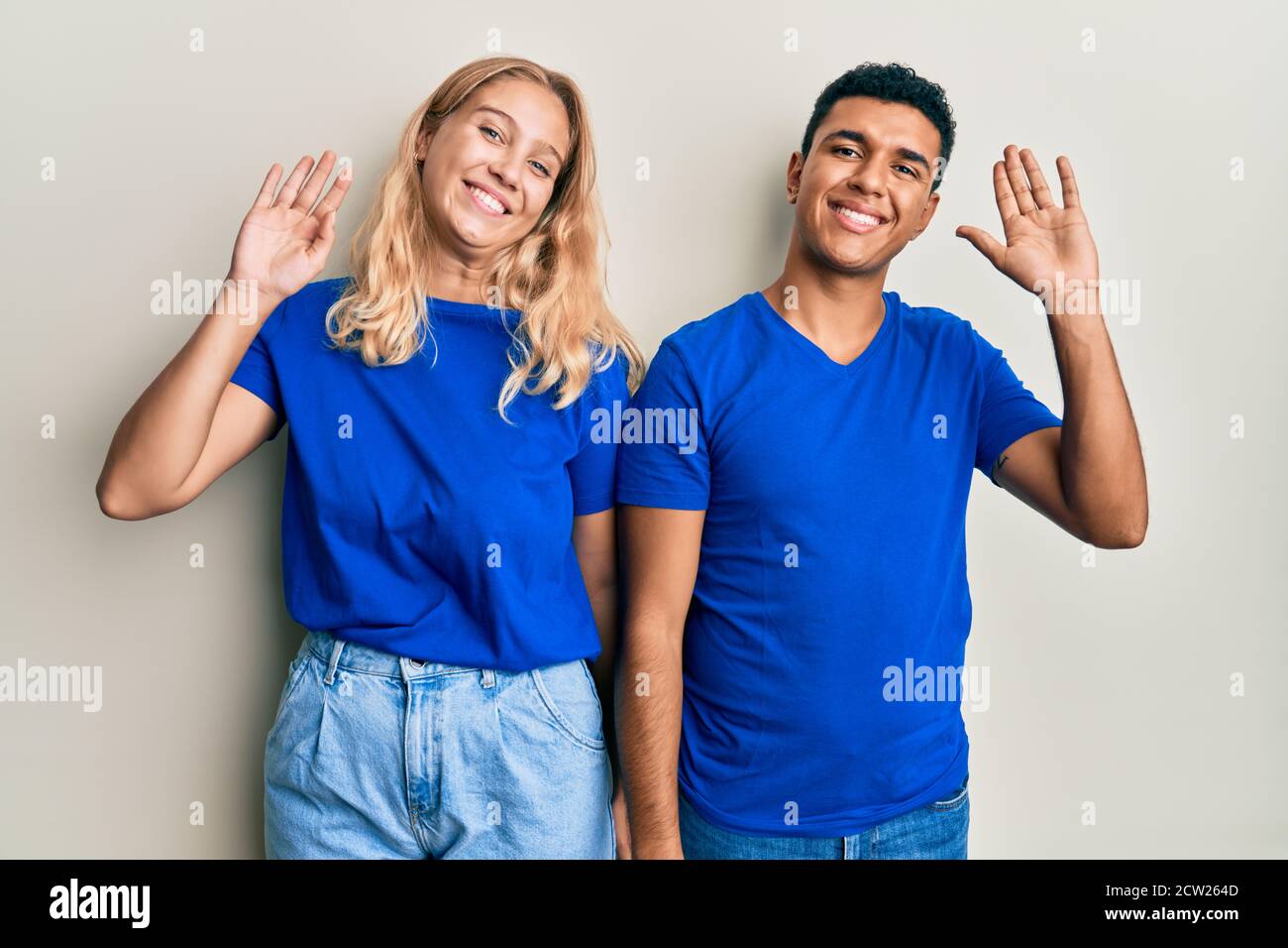 Young interracial couple wearing casual clothes waiving saying hello ...
