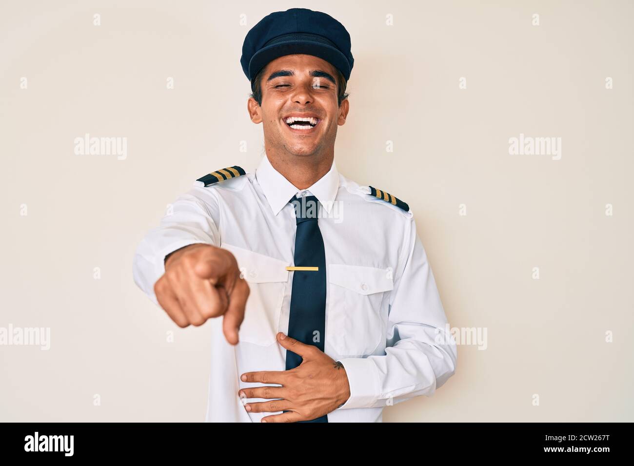 Young hispanic man wearing airplane pilot uniform laughing at you ...