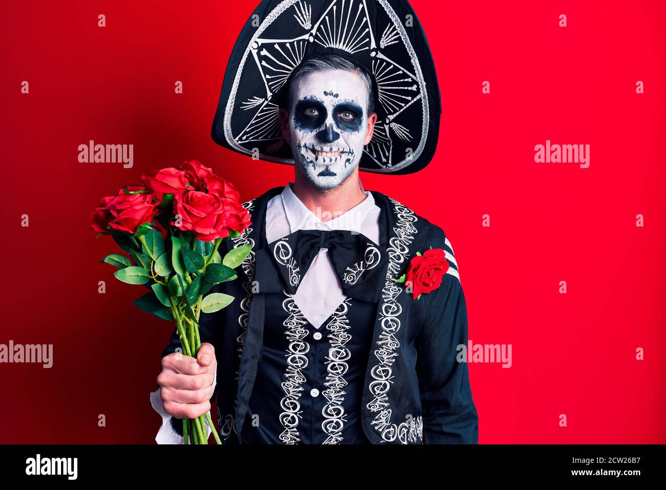 Young man wearing mexican day of the dead costume holding roses looking ...