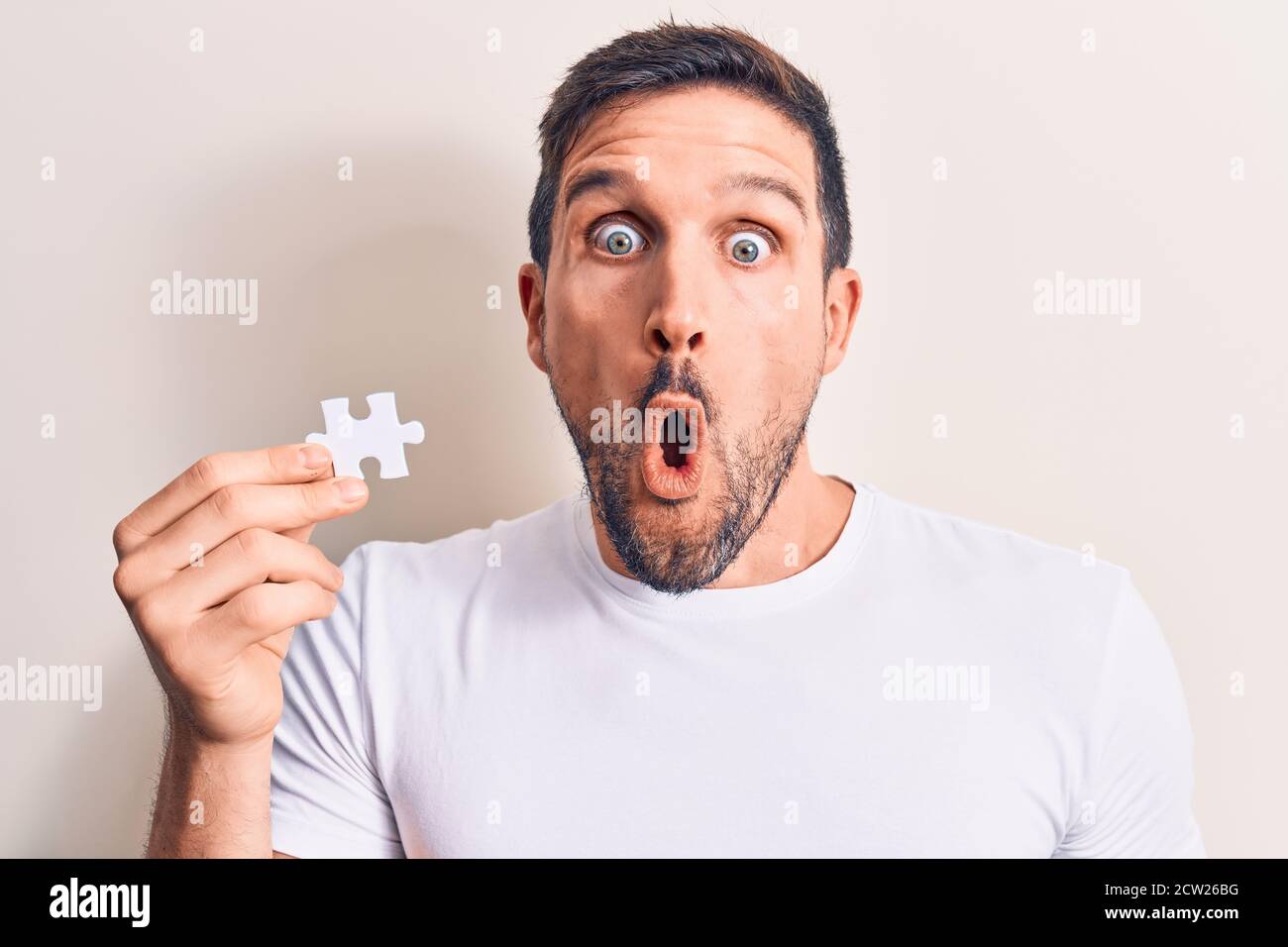 Young handsome man holding piece of puzzle standing over isolated white ...