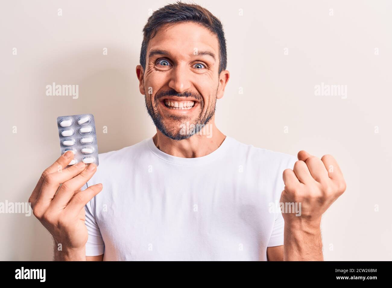 Young handsome man holding medicine pills standing over isolated white ...