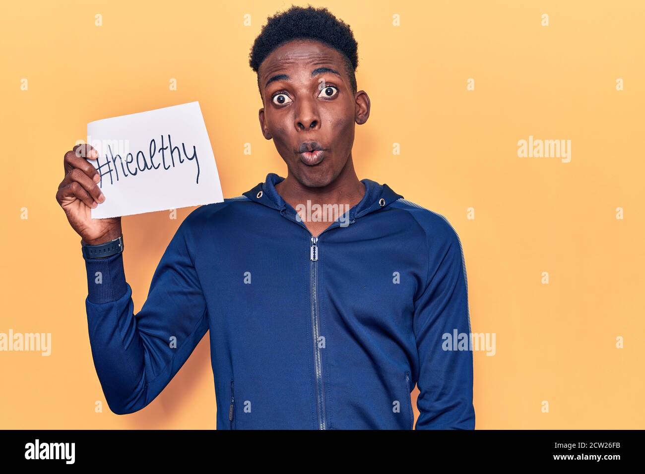 Young african american man holding healthy hashtag paper scared and ...