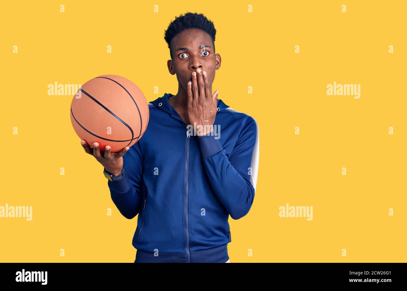 Young african american man holding basketball ball covering mouth with ...