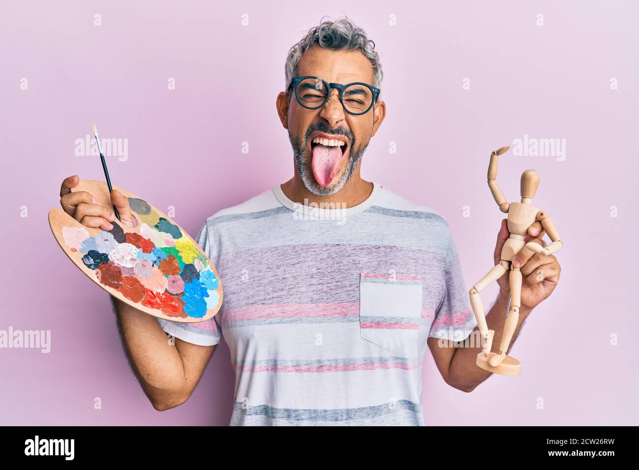 Middle age grey-haired man holding palette and manikin sticking tongue ...