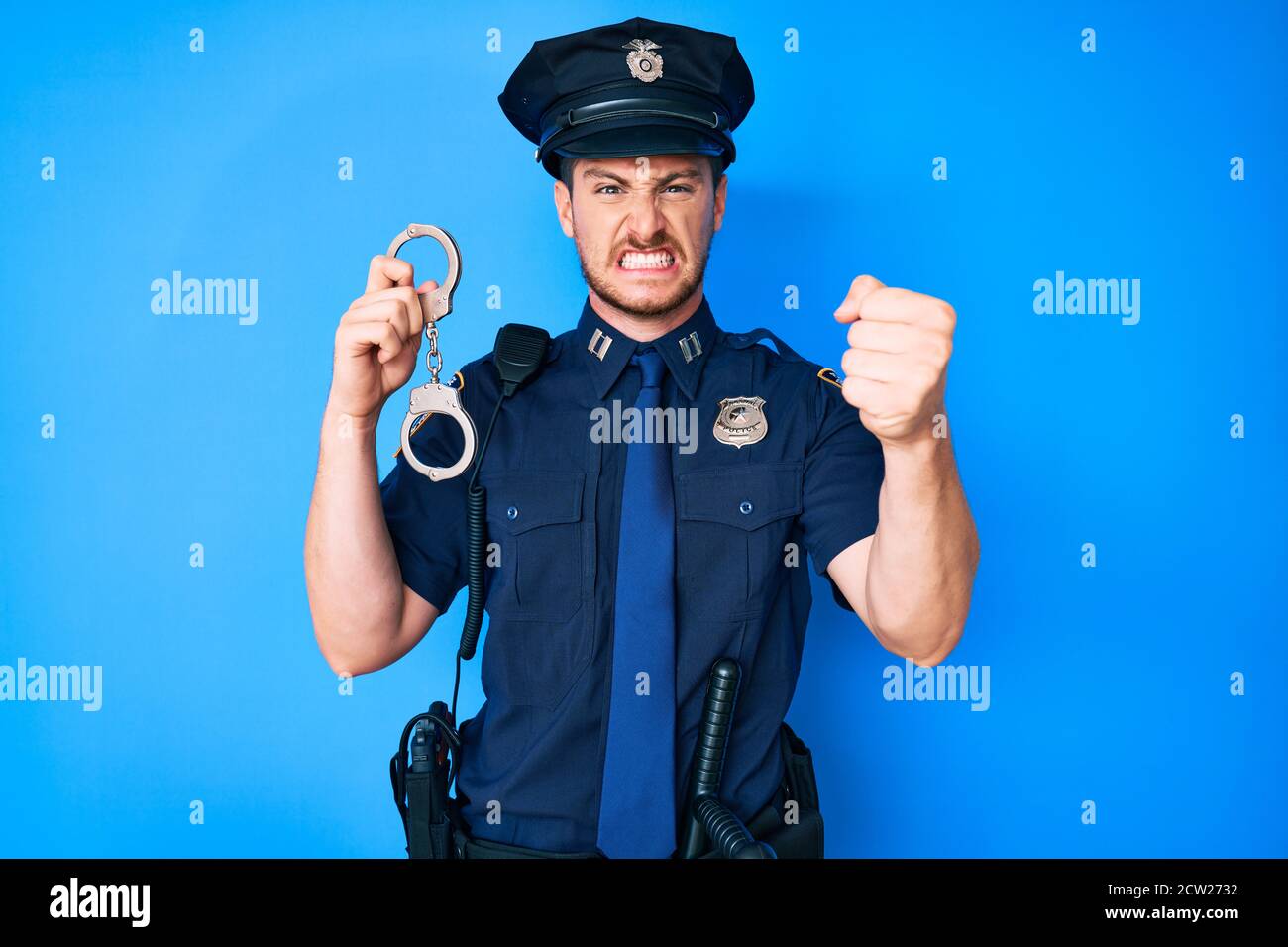 Young caucasian man wearing police uniform holding handcuffs annoyed ...