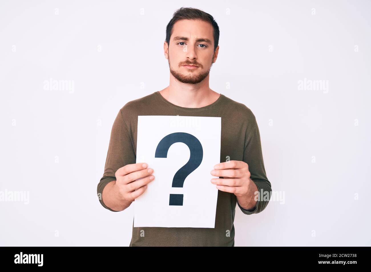 Young handsome man holding question mark thinking attitude and sober ...