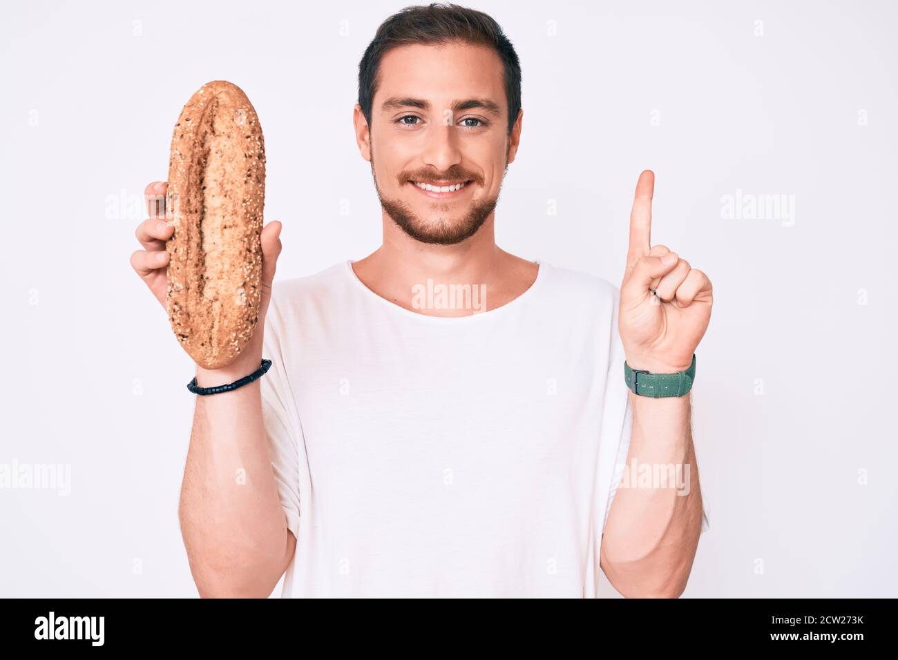 Young handsome man holding wholemeal bread smiling with an idea or question pointing finger with ...