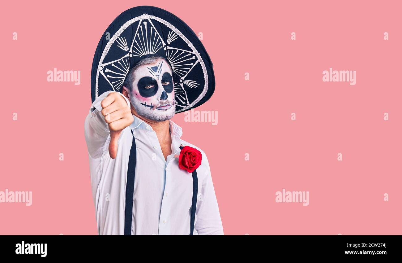 Man wearing day of the dead costume over background looking unhappy and ...