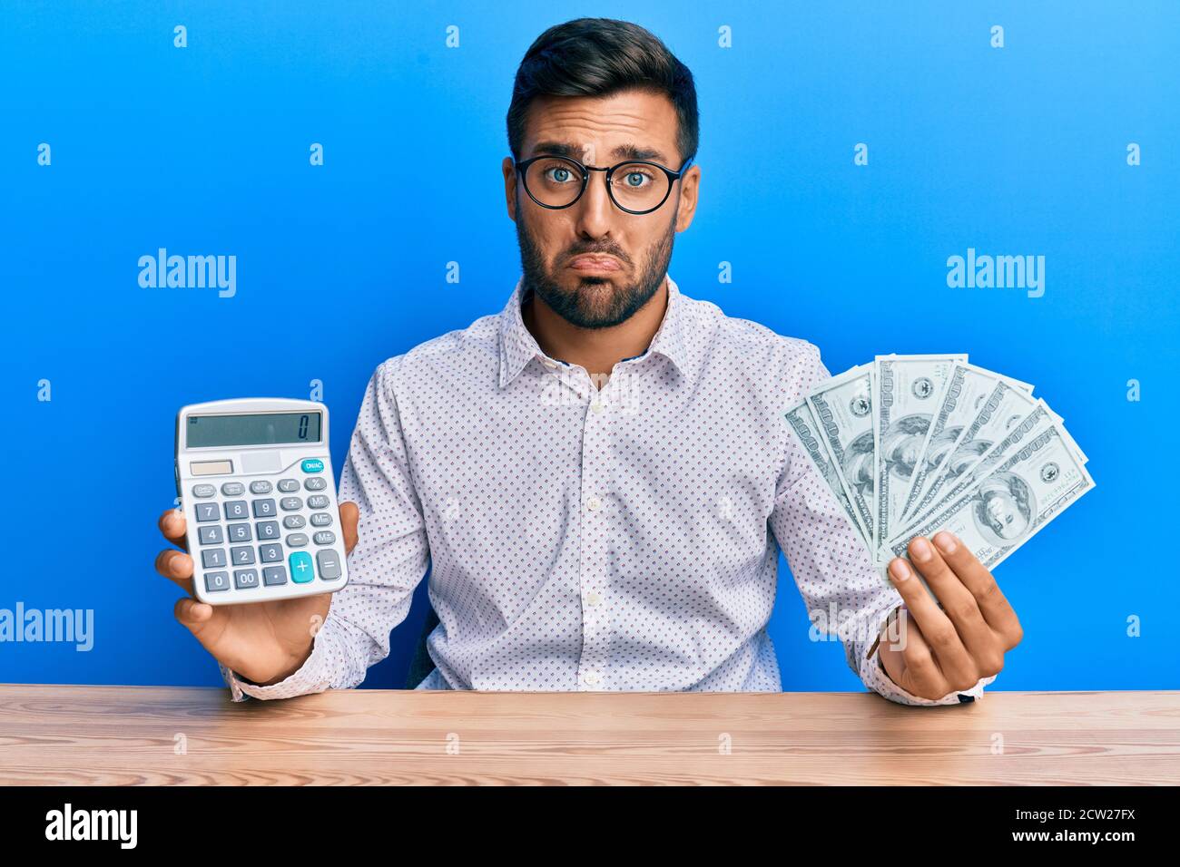 Handsome hispanic man holding dollars calculating savings depressed and ...