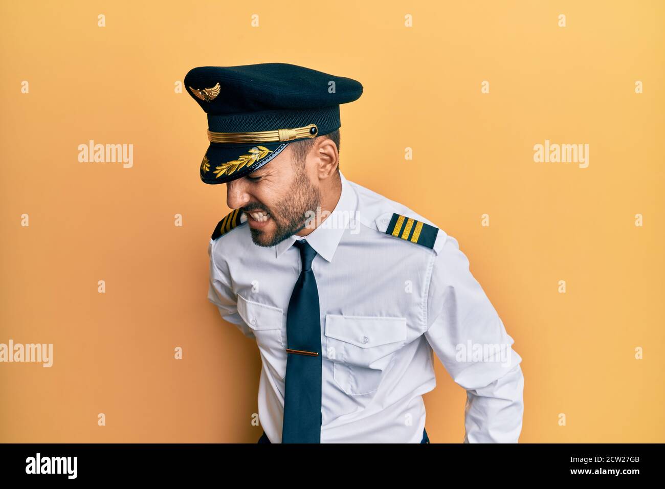 Handsome hispanic man wearing airplane pilot uniform suffering of ...