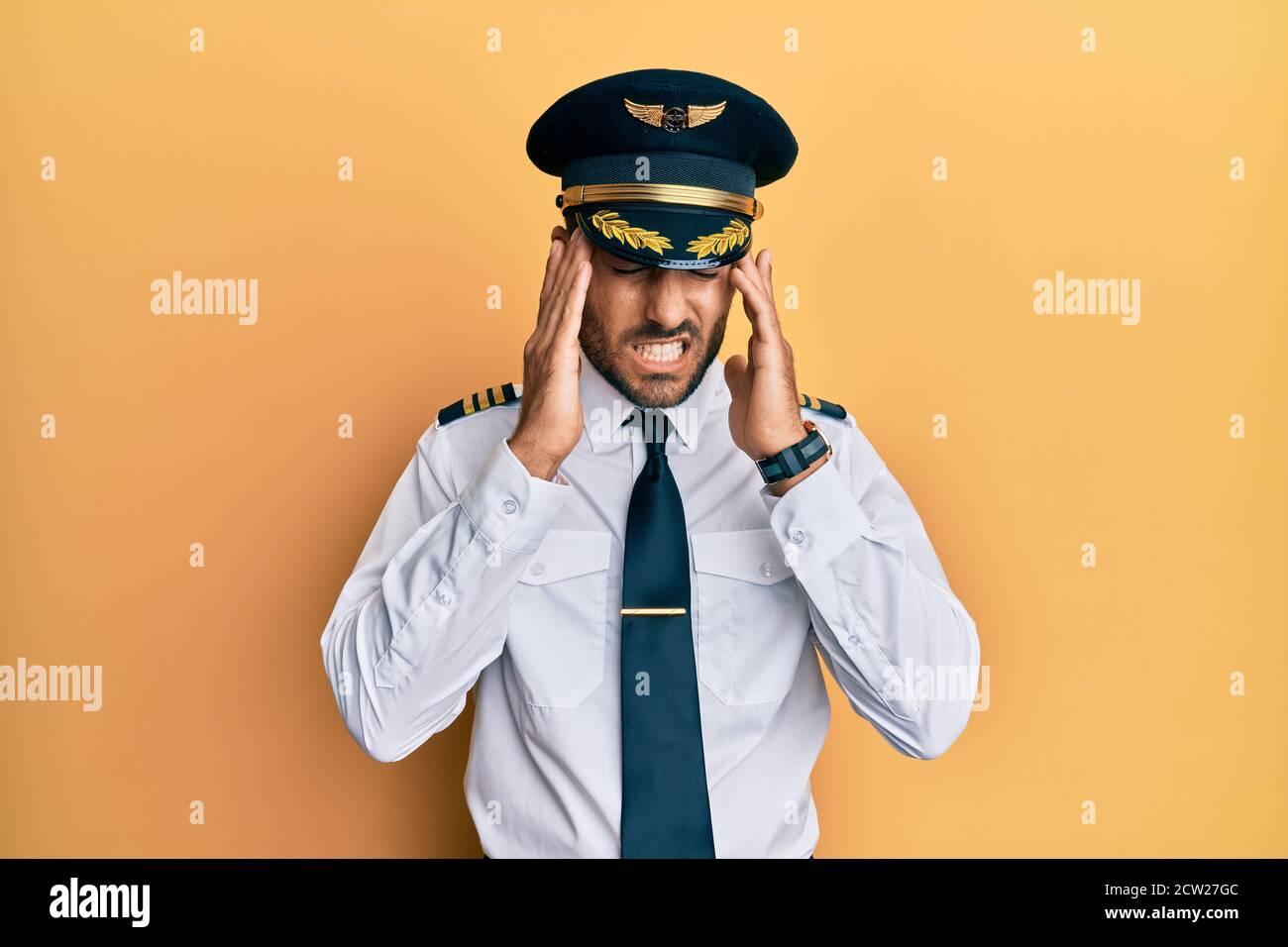 Handsome hispanic man wearing airplane pilot uniform with hand on head ...
