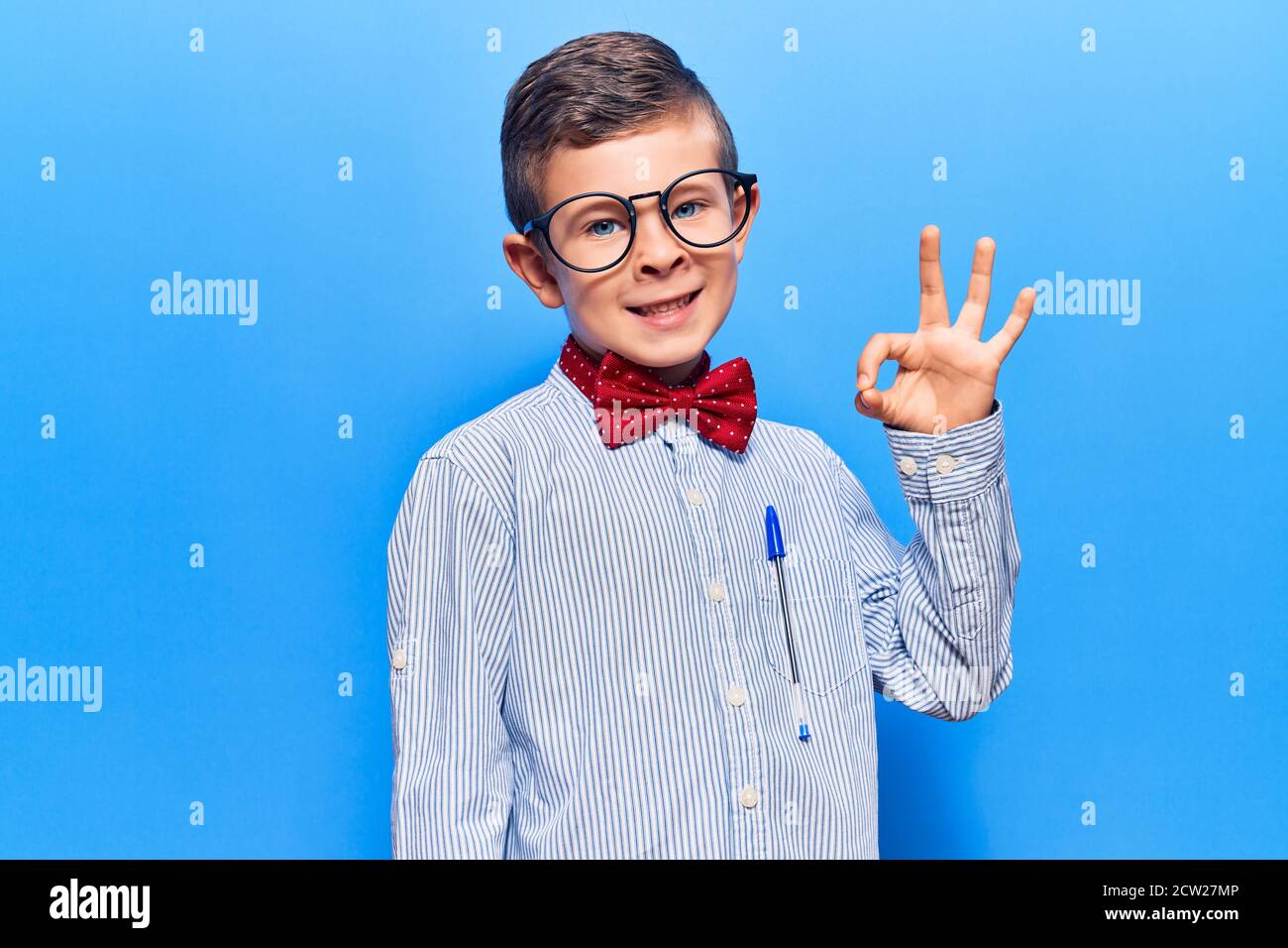 Cute blond kid wearing nerd bow tie and glasses smiling positive doing ok sign with hand and ...
