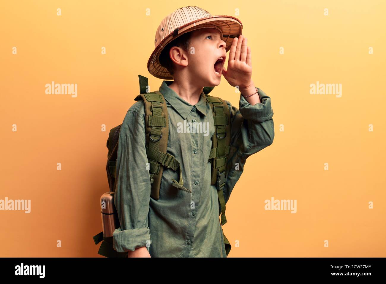 Cute blond kid wearing explorer hat and backpack shouting and screaming ...